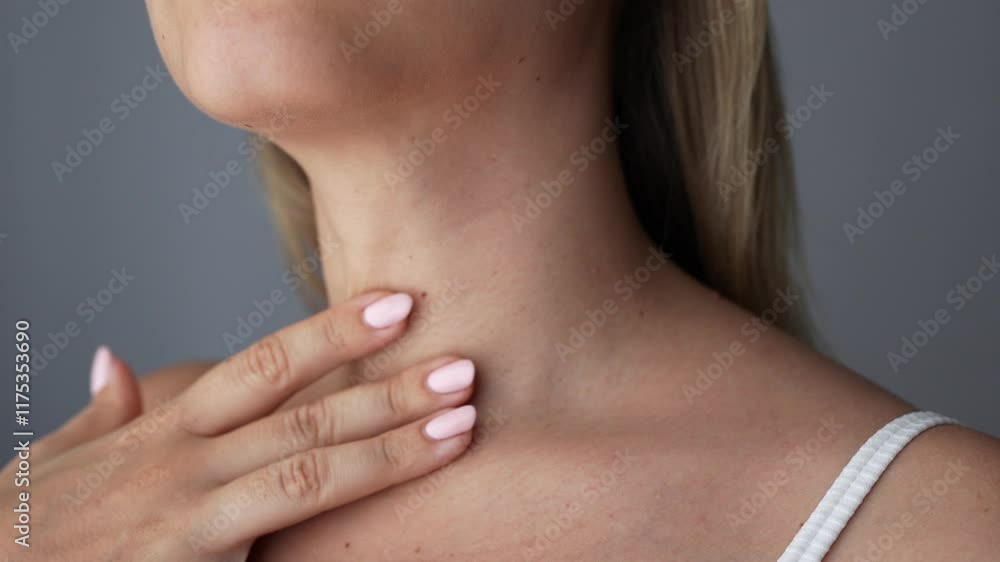Young blonde woman touching her neck with her hand on a dark grey ...