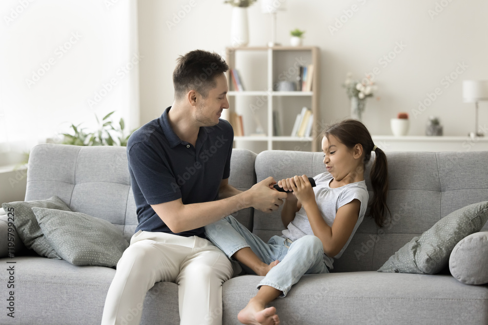 Poster Serious father and little daughter sit on sofa grabbing ...