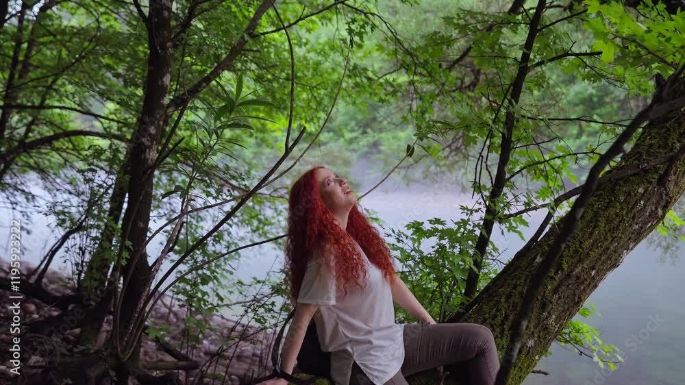 Happy adult female sitting on a trunk tree in forest woods enjoy wild ...