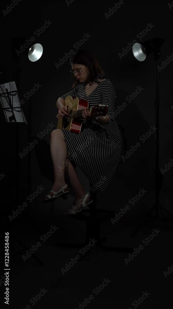 Young woman guitarist playing guitar sitting on bar stool in flickering ...