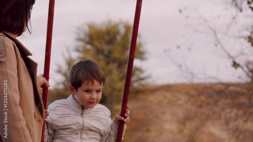 Smiling mother swings son on swing adding atmosphere. Mother amid ...