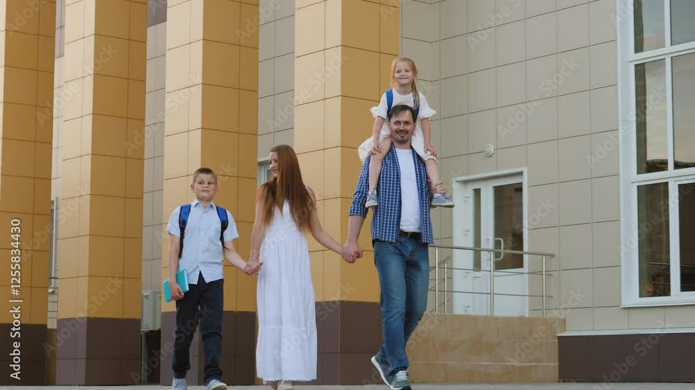 Cheerful family takes little children to school walking past building ...