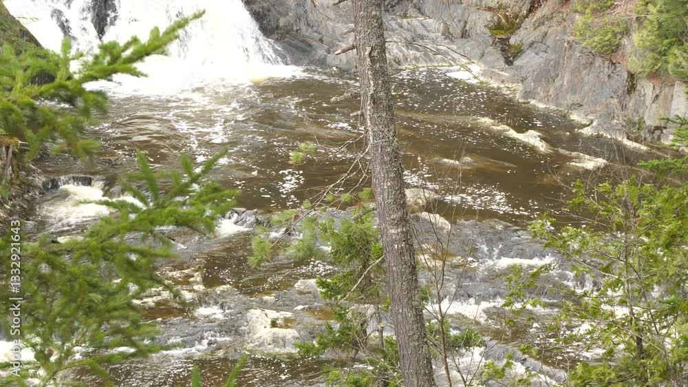 At the base of a powerful waterfall pouring into a river with a ...