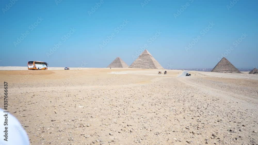 A wide desert view of the Giza Pyramids in Egypt, with a tour bus and ...