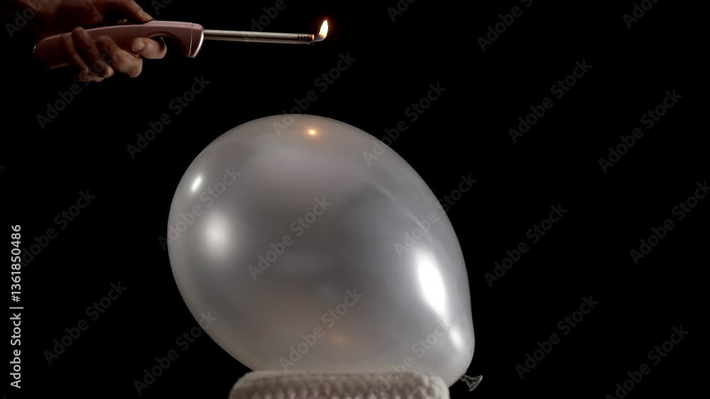 A silver balloon rests still as a hand lights a small flame on a ...