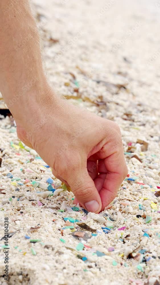 A hand picking up a piece of microplastics from a beach, sand mixed ...