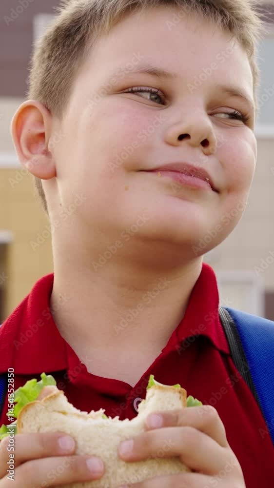 child kid boy eats sandwich with a school backpack on her back ...