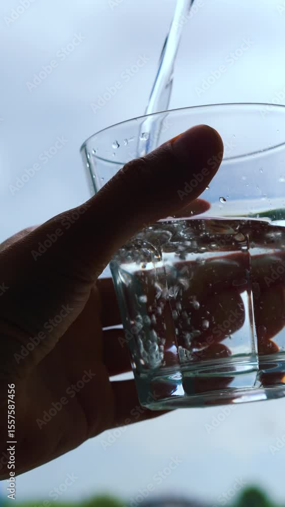 A person pours clean, potable water into a transparent glass. Water on ...
