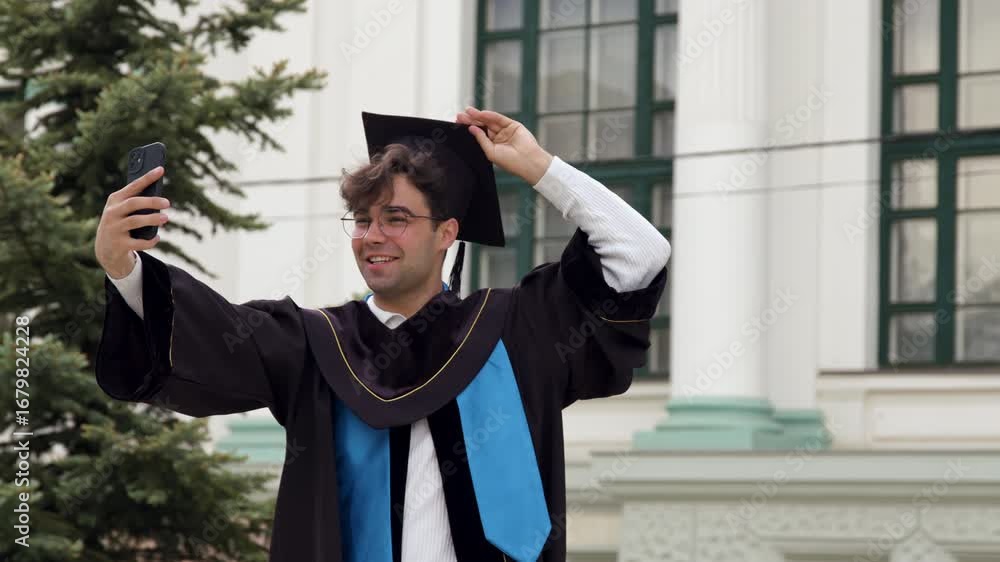 Modern graduate boy with cap and gown. Young man talks online with ...