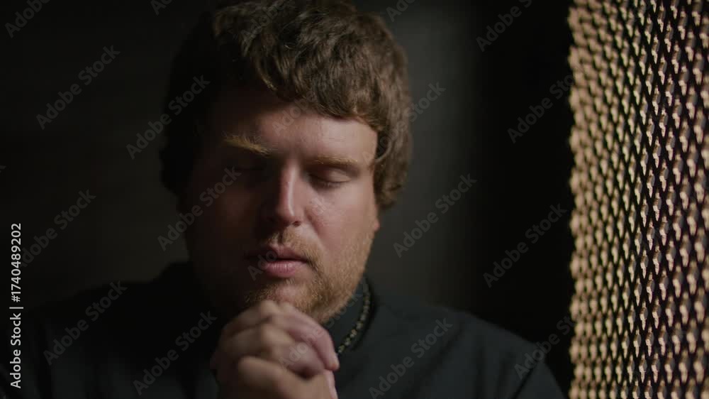 Young priest holding hands together and praying with eyes closed while ...