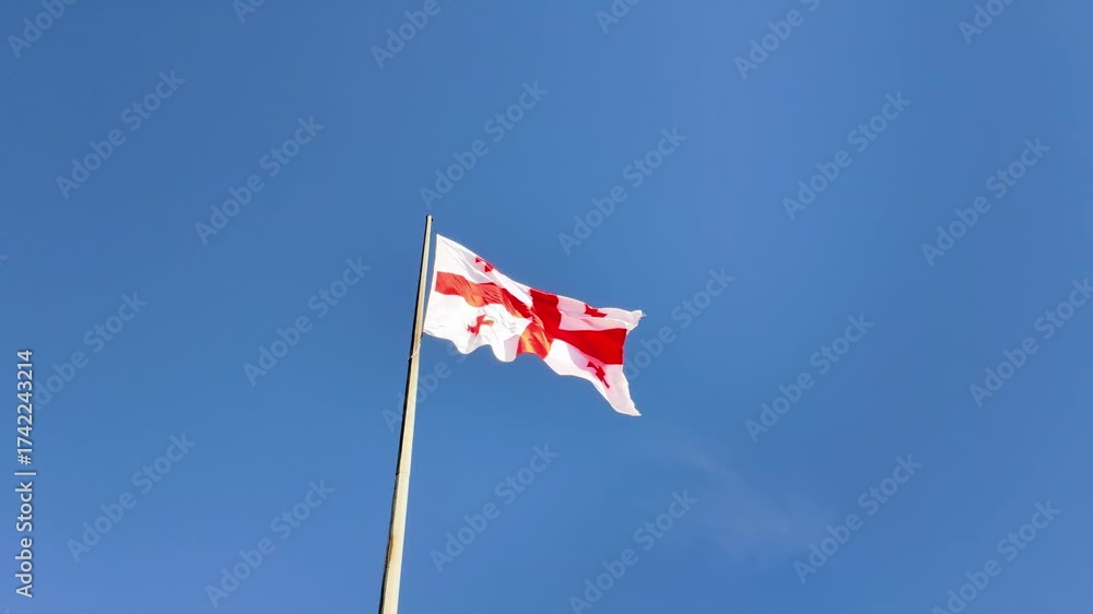 The national flag of Georgia waves proudly against a clear blue sky ...