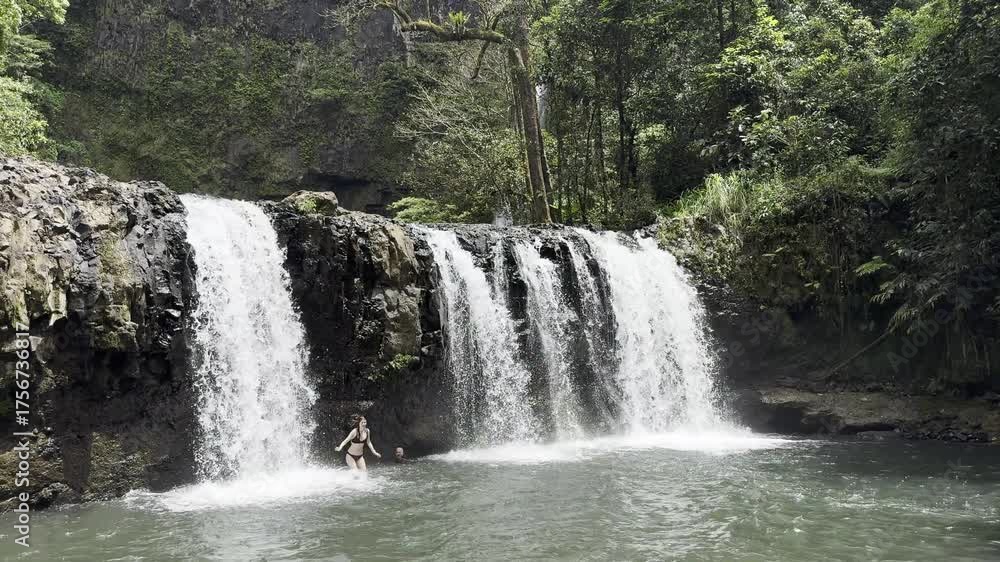 brave girl in bikini stands under powerful tall waterfall in dense ...