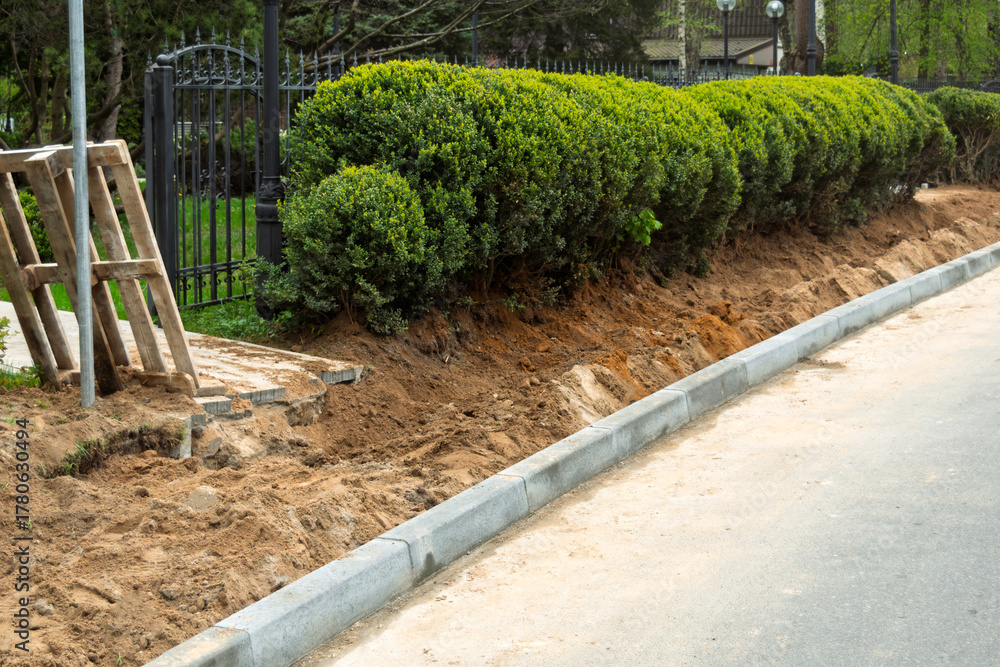 Freshly installed curb separates green bushes and bare soil from ...