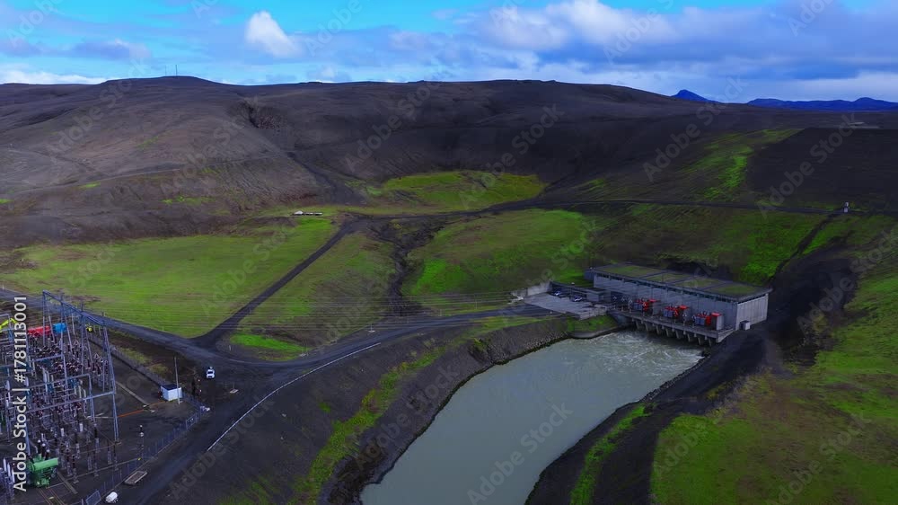 Daylight aerial pans show a concrete powerhouse, active spillway, and ...