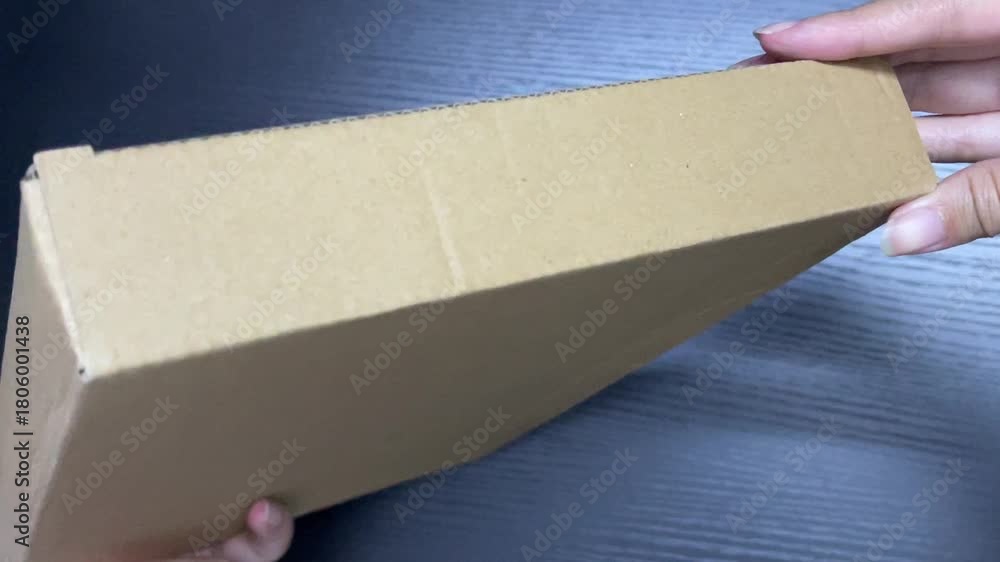 A close up shot of two hands rotating a brown cardboard box to inspect ...