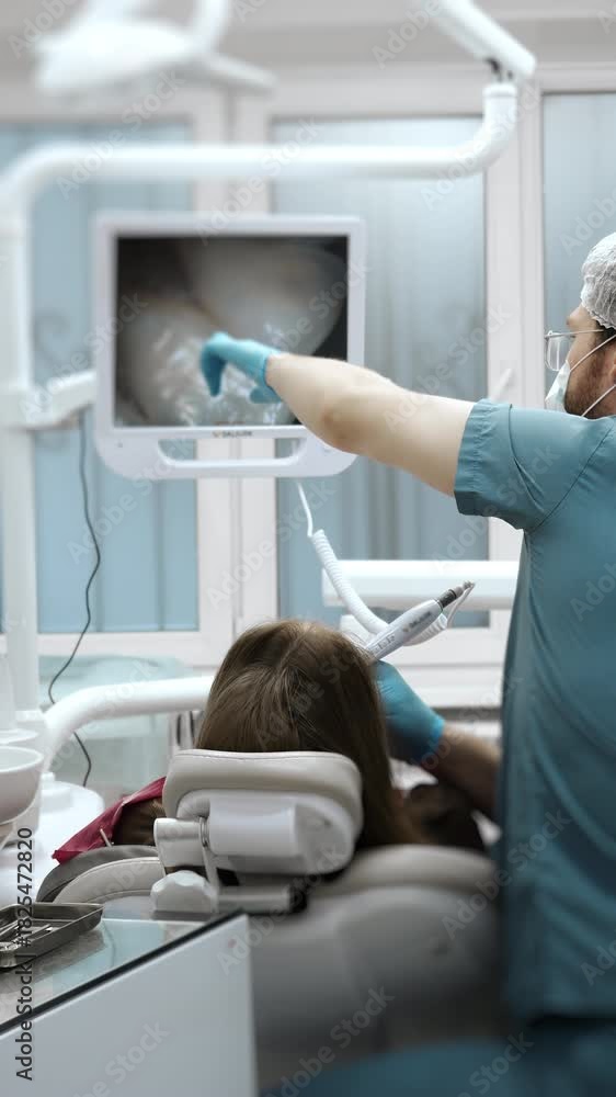 Dentist pointing at a tooth image on a monitor while examining a ...