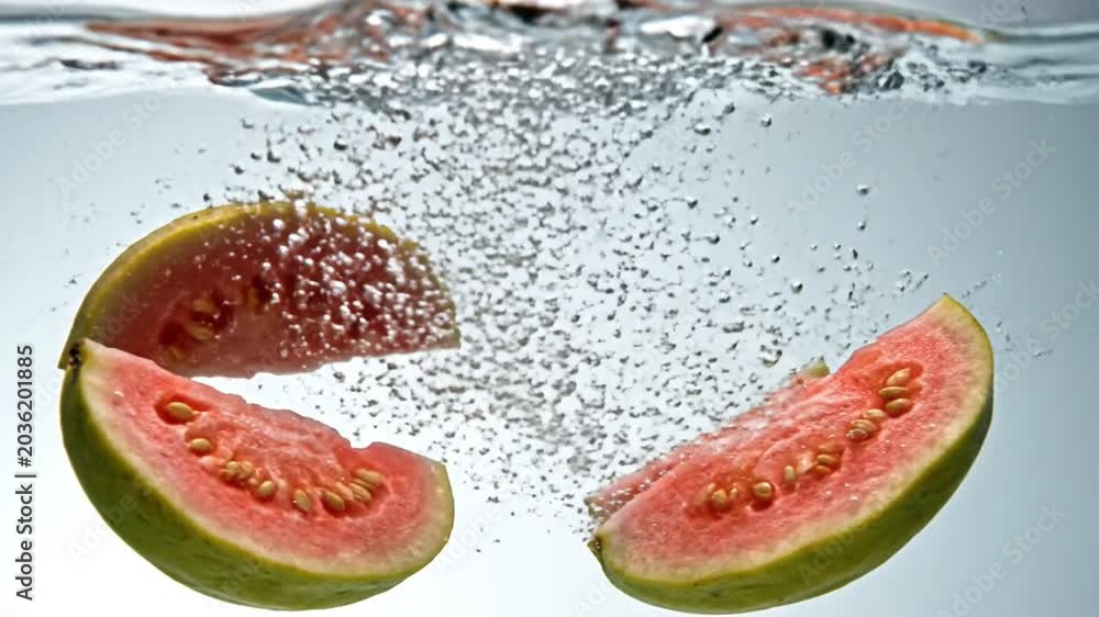Two vibrant pink guava halves splash into clear water, creating a ...