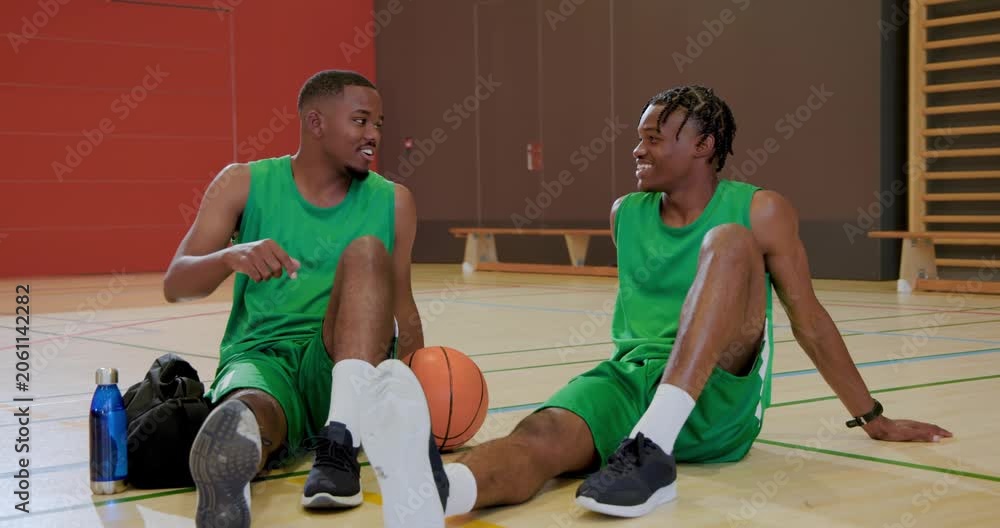 Resting after practice, african american teammates talking on gym floor ...